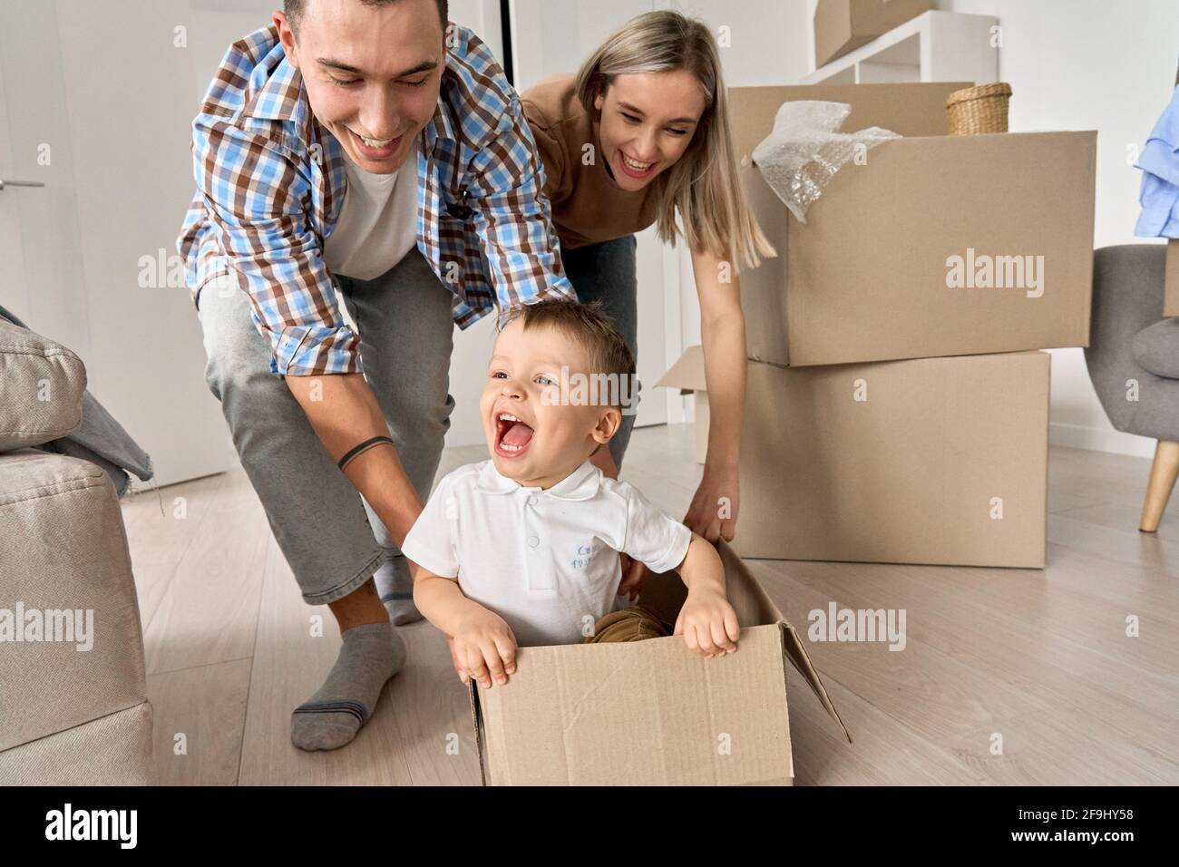 Happy parents playing with cute toddler kid son riding in box on moving ...