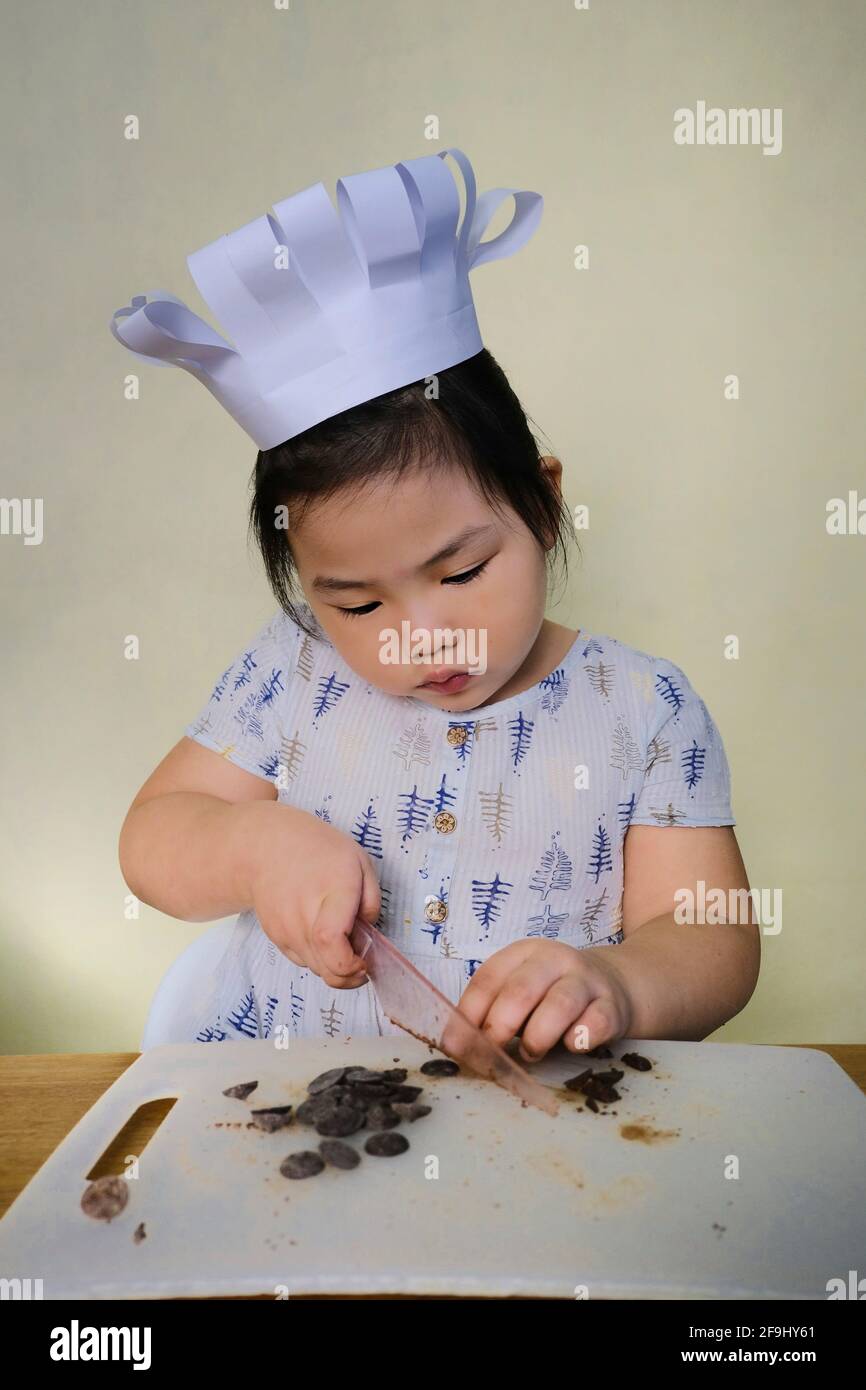 A cute young chubby girl with a chef hat is learning to cook with her ...