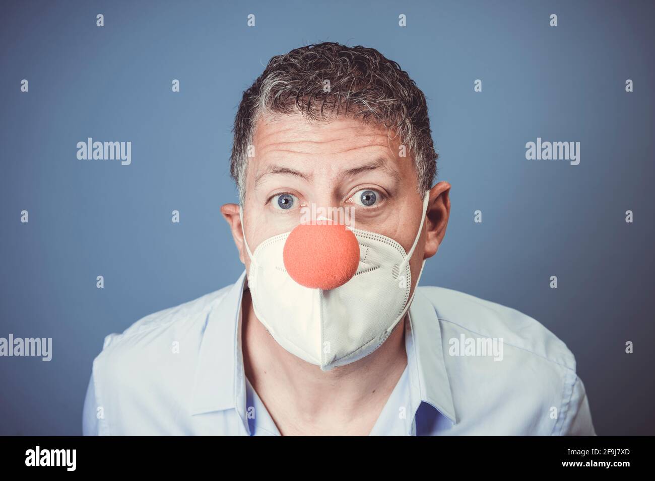 Middle aged man with nose mouth protection and red clown nose in front ...