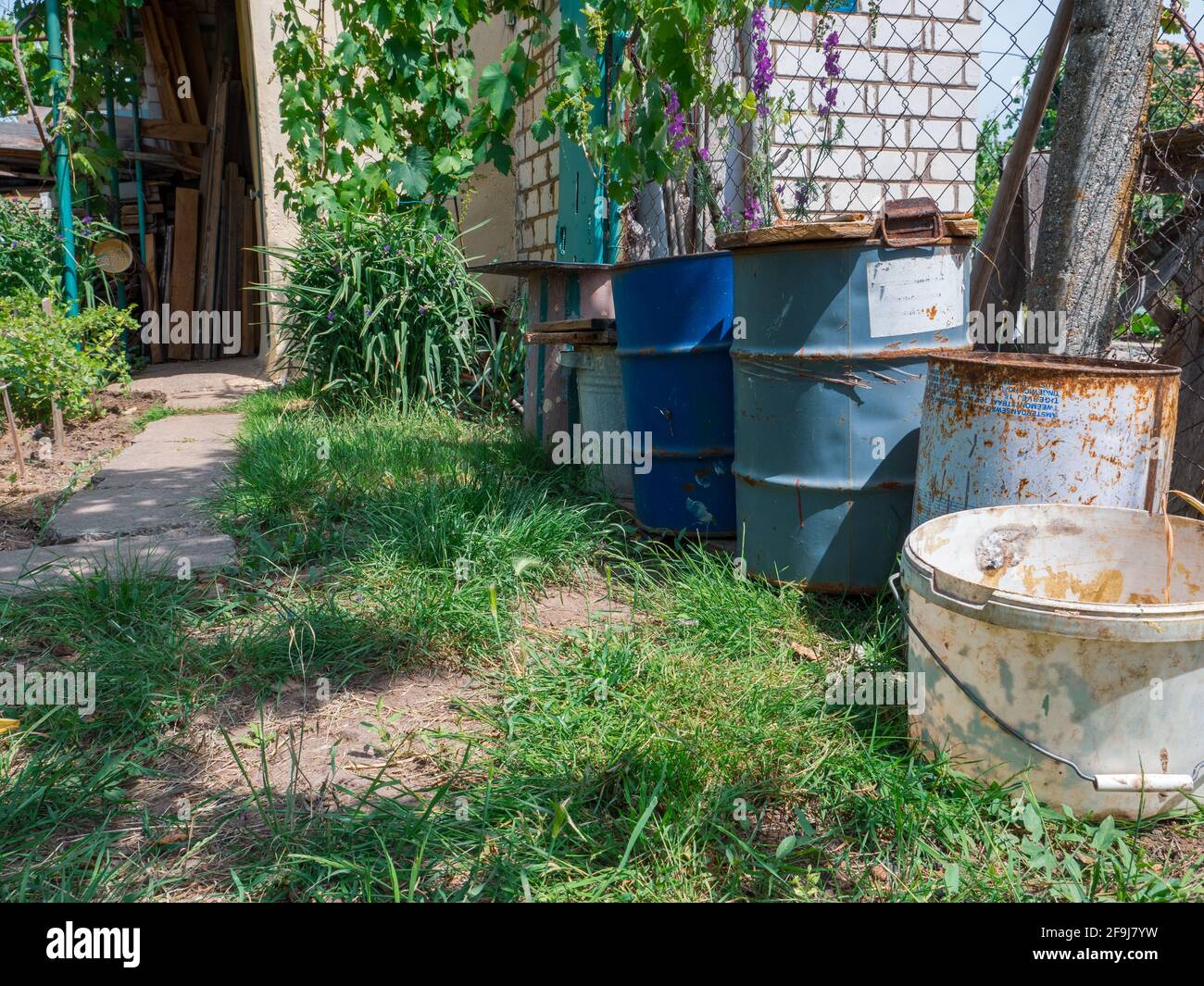 Old rusty metal barrels with wooden lids and plastic buckets as rural ...