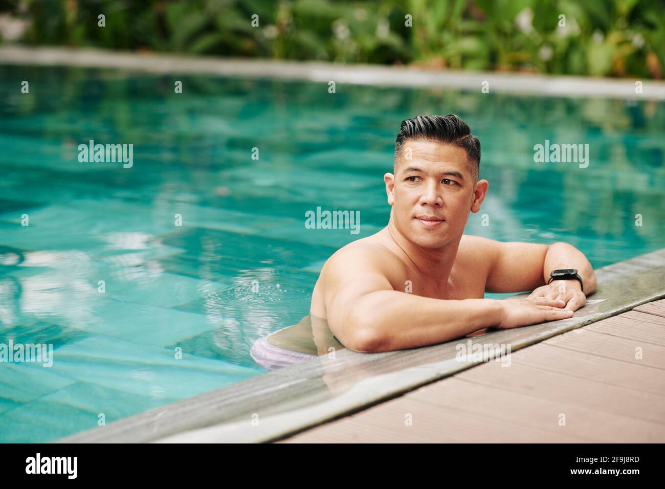 Portrait of handsome fit muscular man standing in swimming pool and ...