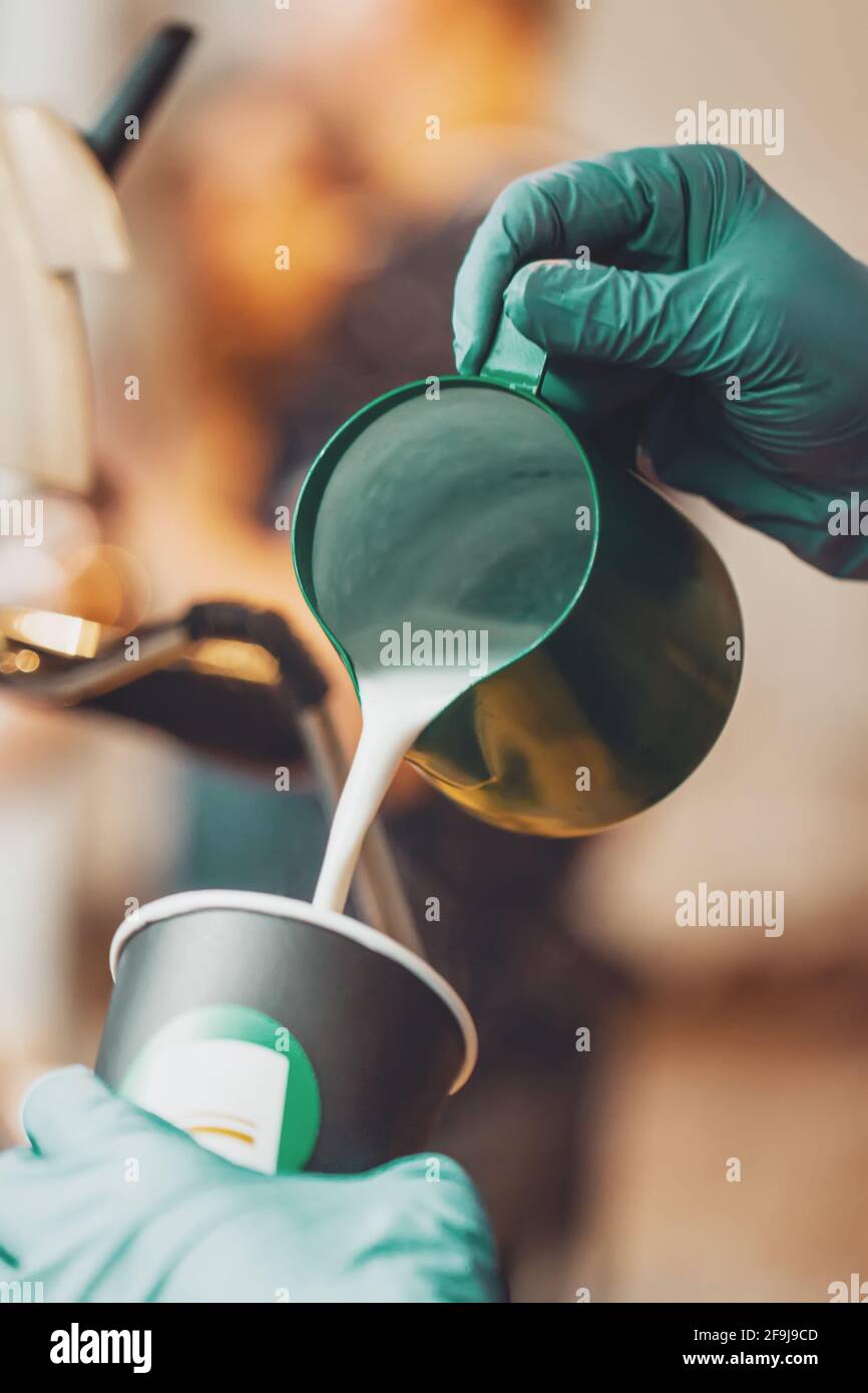 Close-up of barista hands in disposable gloves pouring hot milk with ...