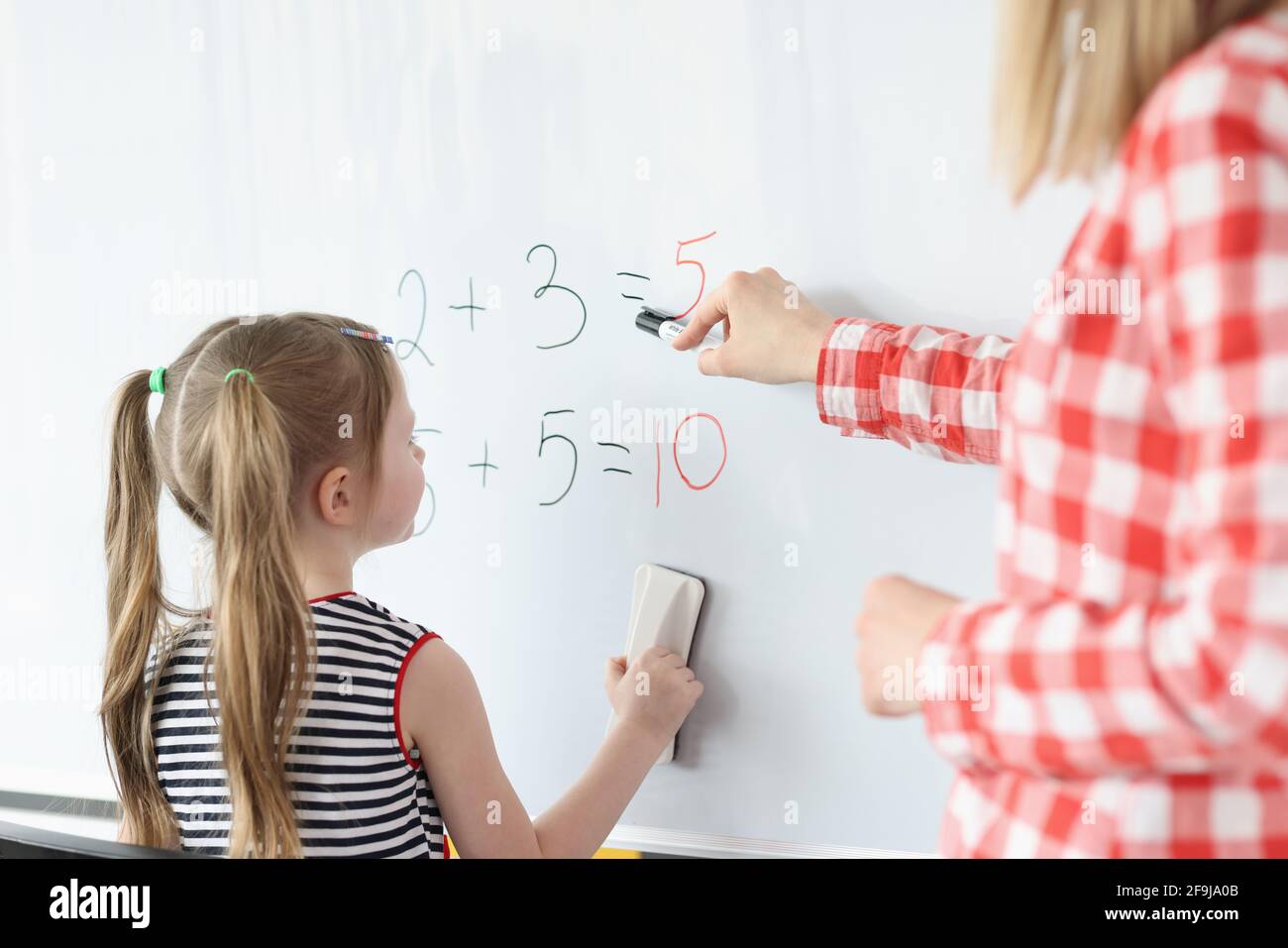 Little girl and teacher solving math equations on blackboard Stock ...