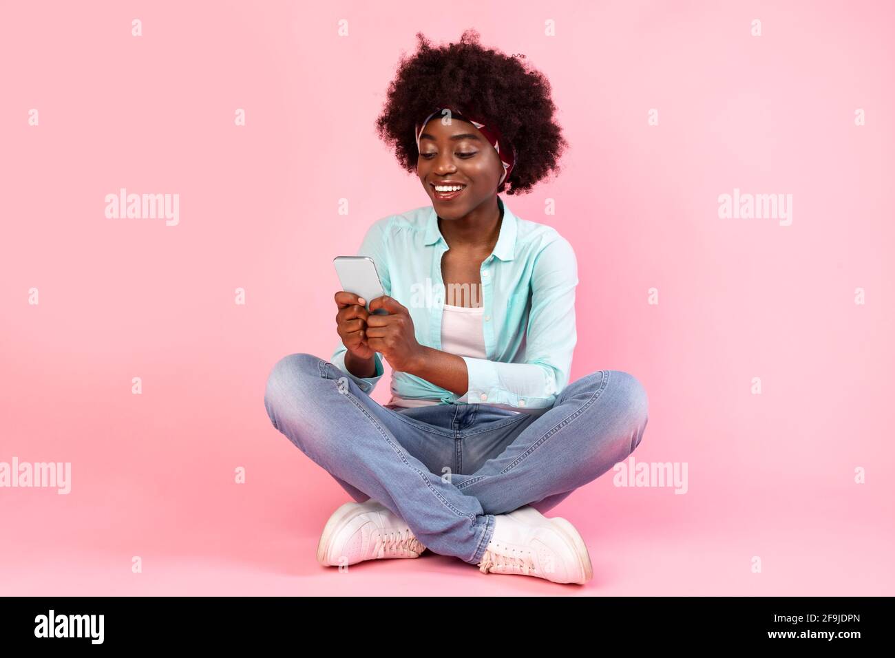 African Woman Using Phone Texting Sitting On Floor, Pink Background ...