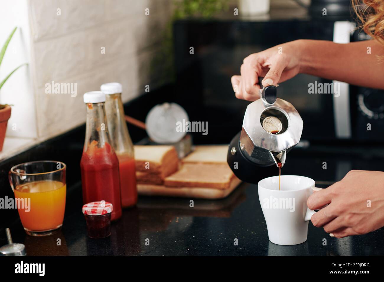 Close-up image of young woman pouring coffee in cup when making herself ...