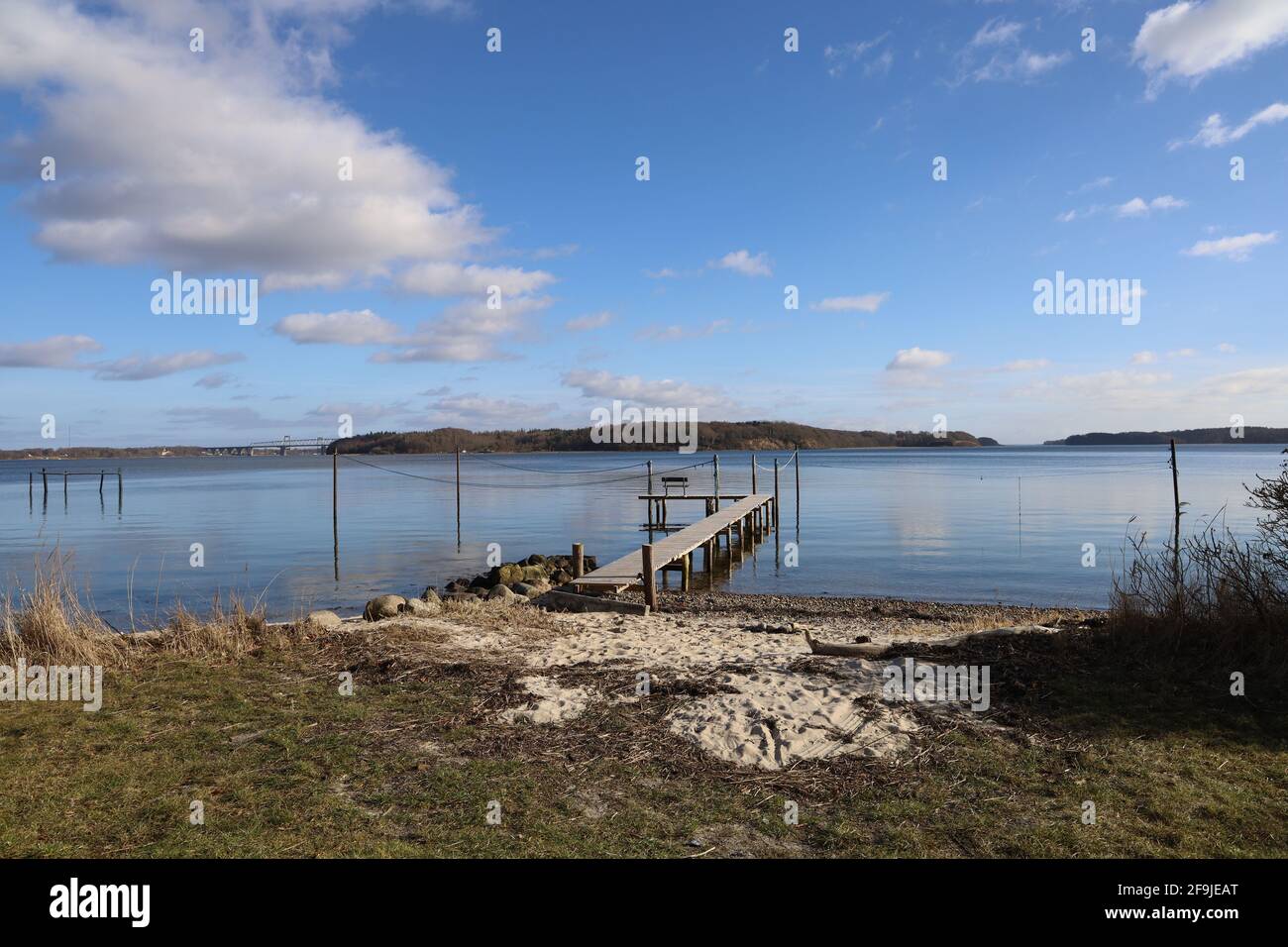 Wooden dock on a lake surrounded by fields under a blue cloudy sky in ...