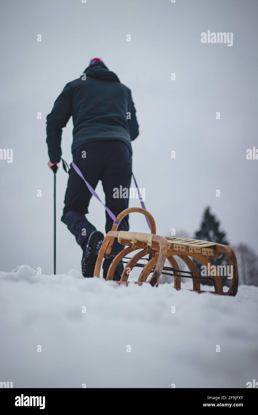Athlete in black winter clothes pulls to the top of the slope a wooden ...