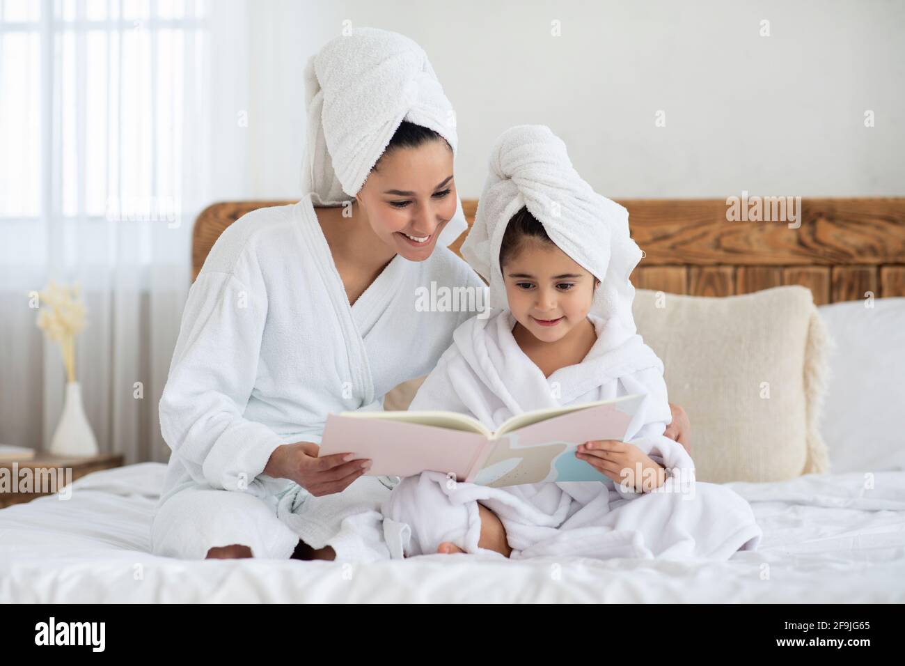 Joyful mother and daughter in bathrobes reading fairy tales Stock Photo ...