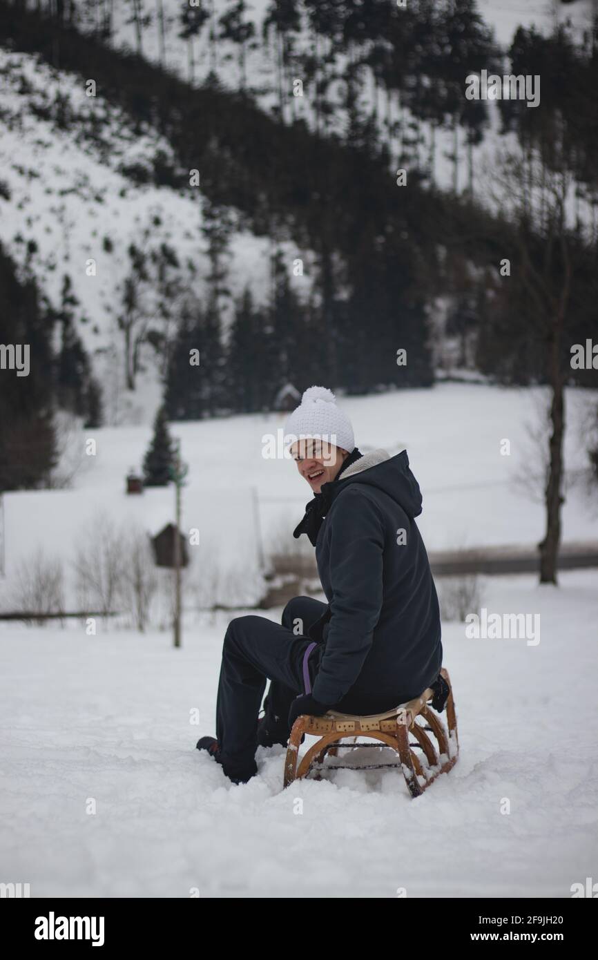 Teenager with a smile on his face sits on a wooden historic sledge and ...
