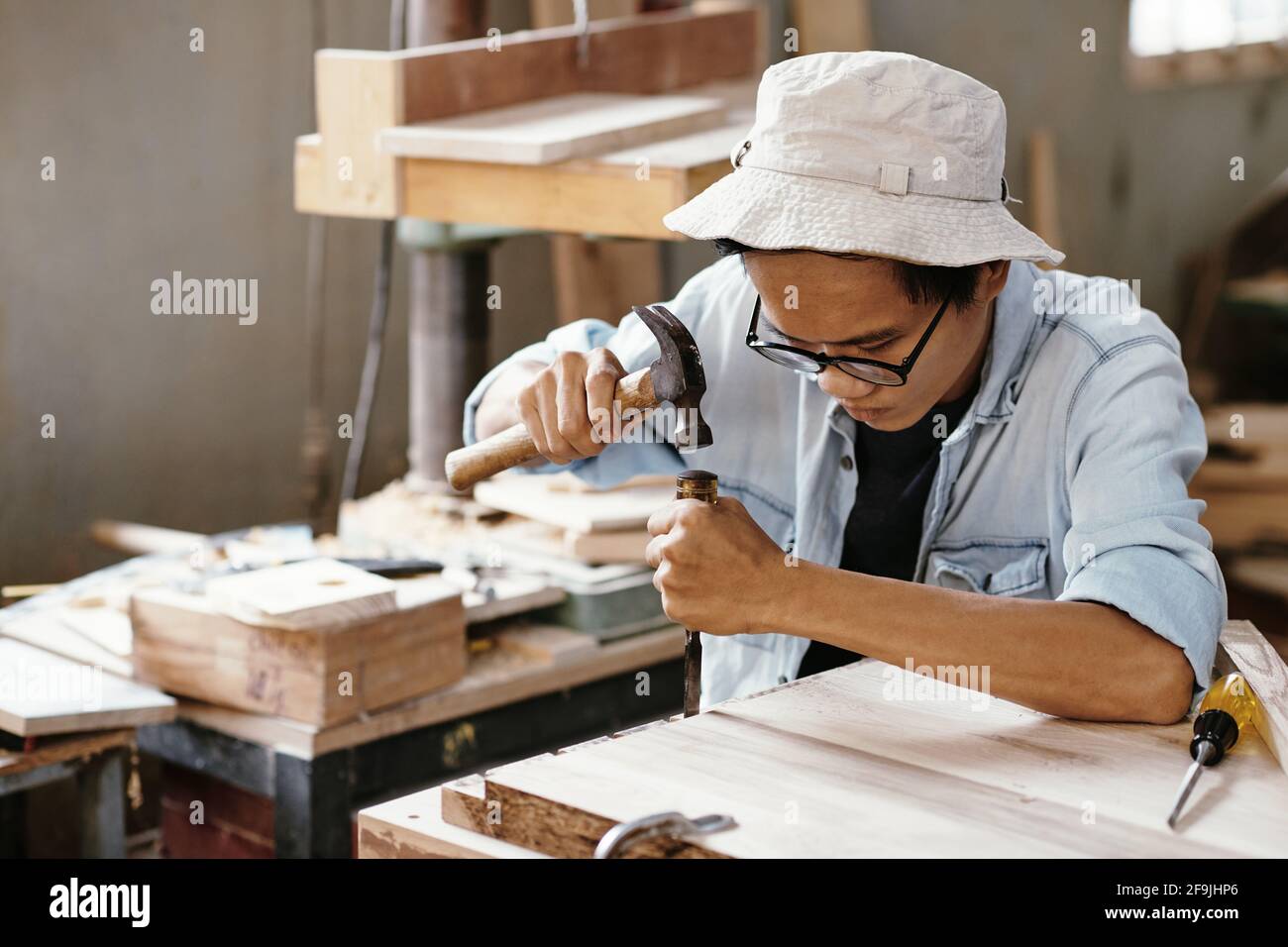 Concentrated young Asian man using chisel and hammer when working with ...