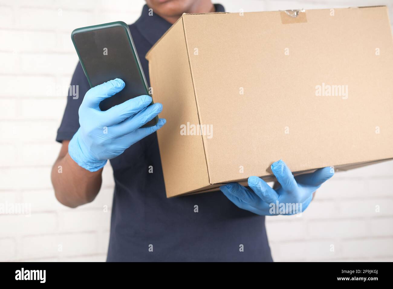 delivery man hand in latex gloves holding smart phone and card box ...