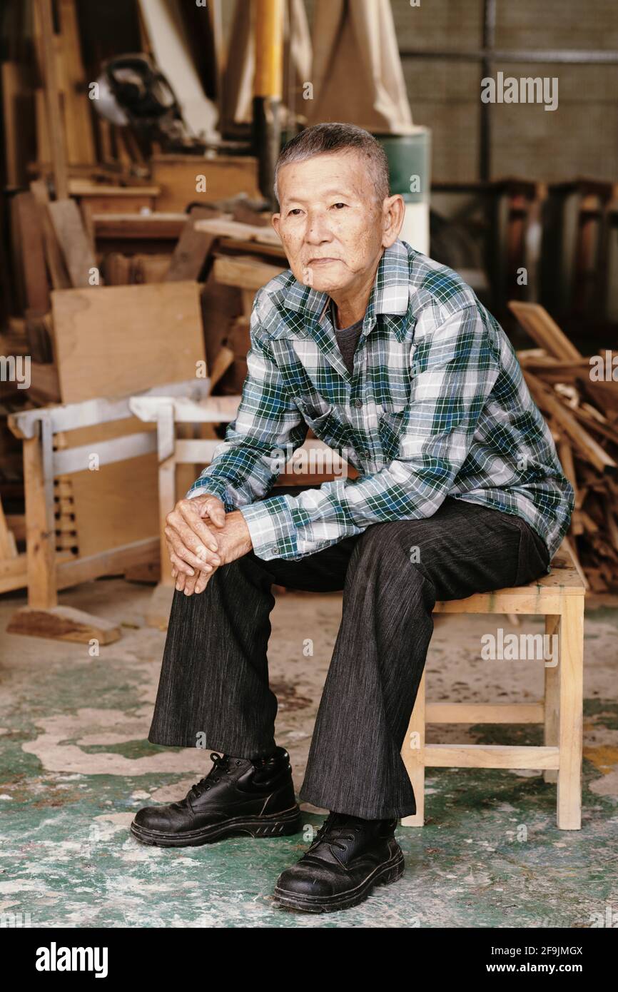 Contemplating senior Vietnamese carpenter sitting on stool in his ...