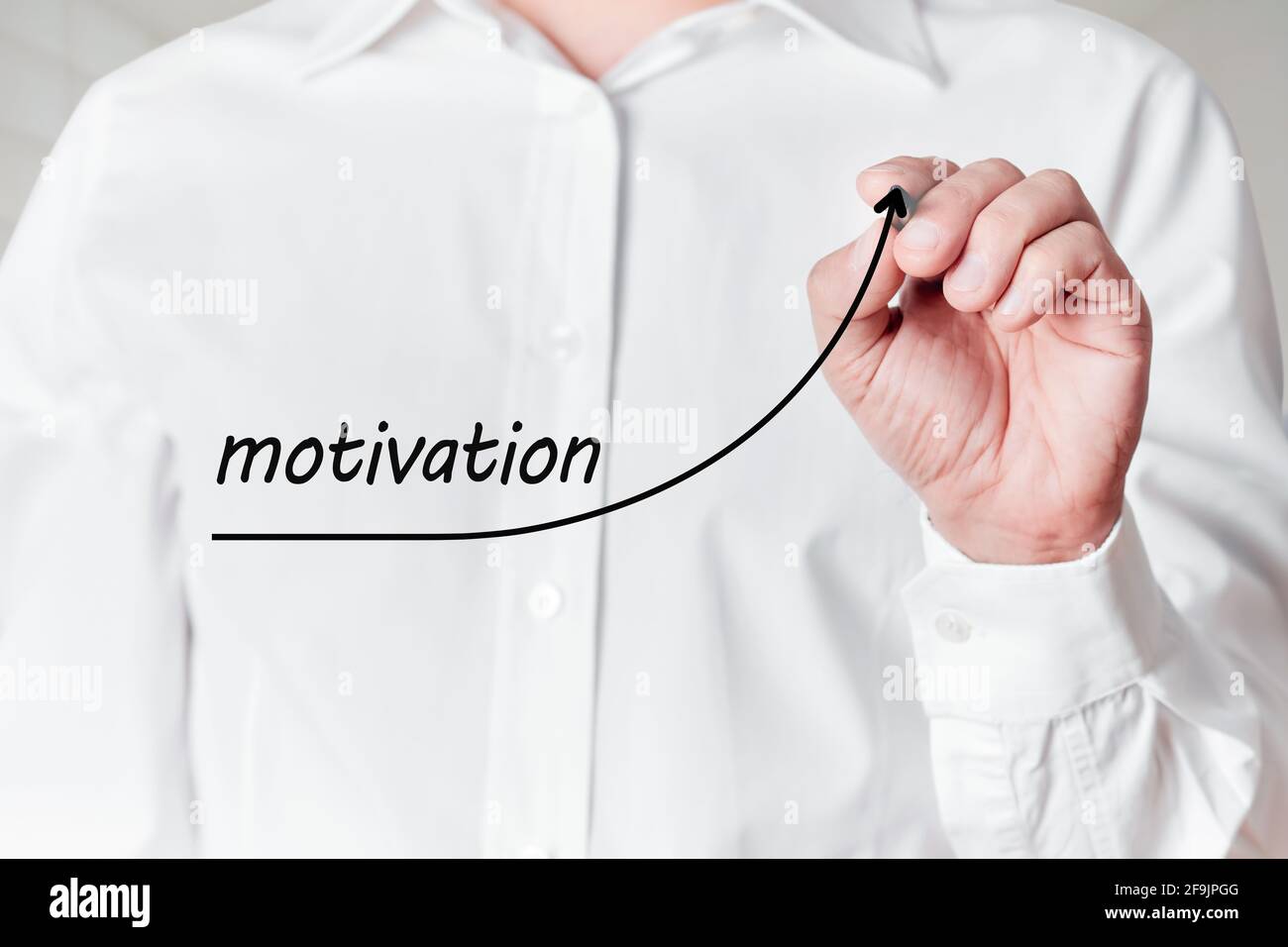 Businessman with pen draws a rising line graph with the word motivation ...