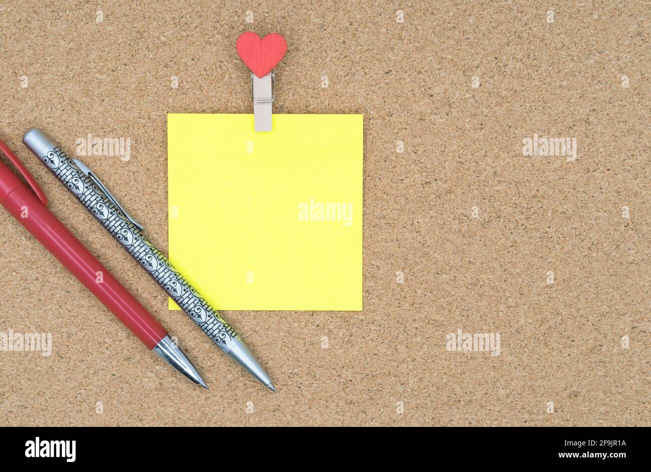 Yellow sticker with clothespin and ballpoint pens on a cork board Stock ...
