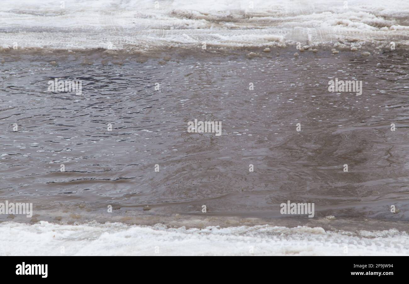 A deep puddle of ice and snow along the edges on the road in the city ...