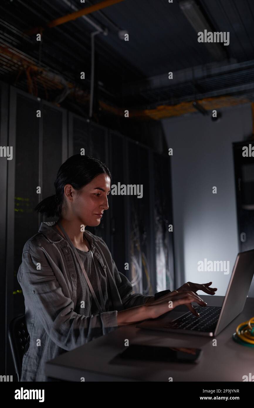 Vertical side view portrait of female network engineer using laptop ...