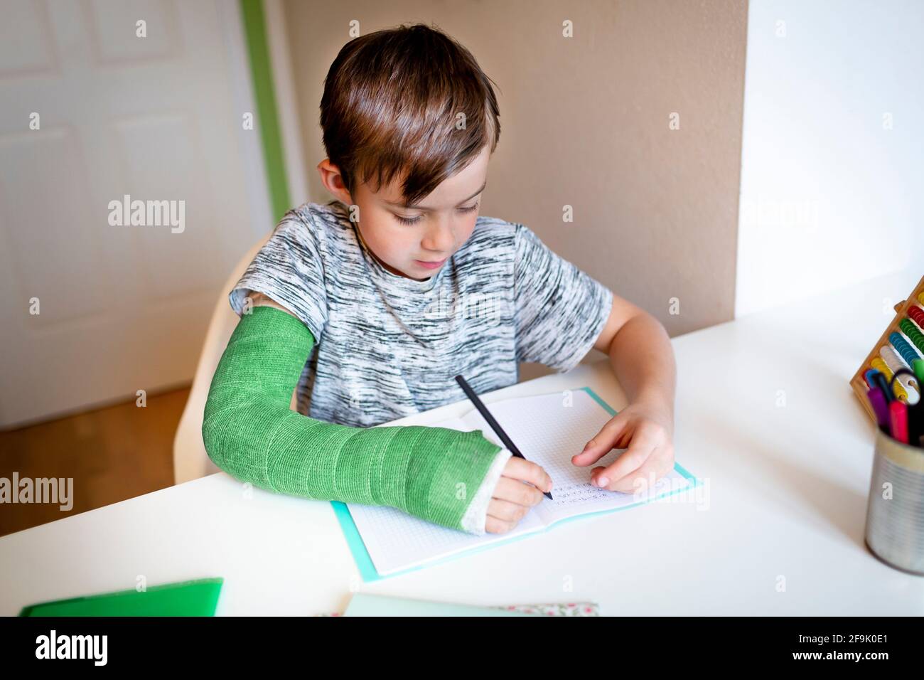 cool boy with green arm cast is sitting in his room and is writing ...
