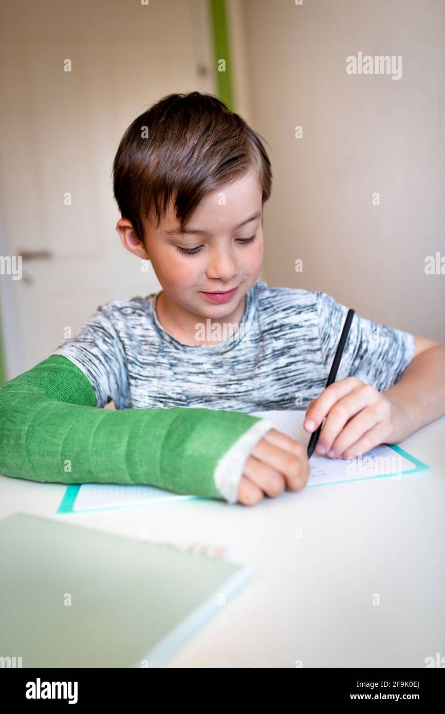 cool boy with green arm cast is sitting in his room and is writing ...