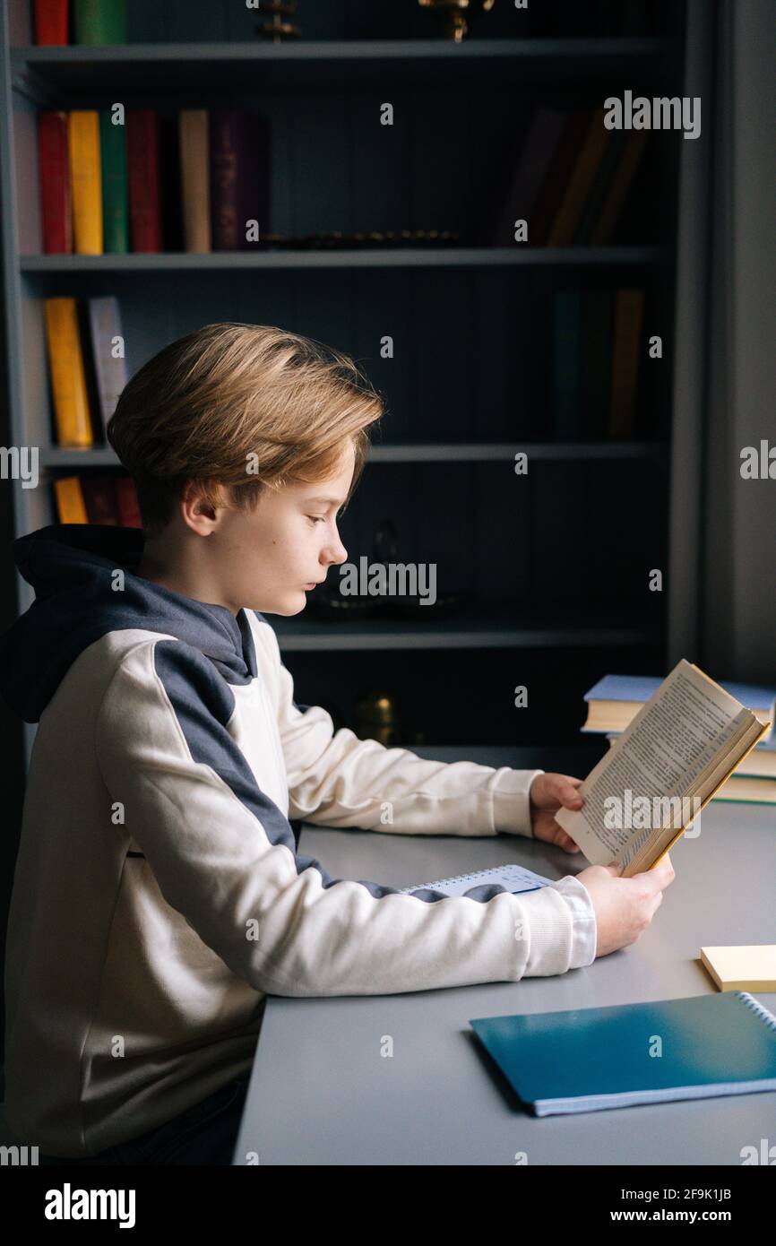 Side view of smart pupil boy reading paper study book sitting at desk ...