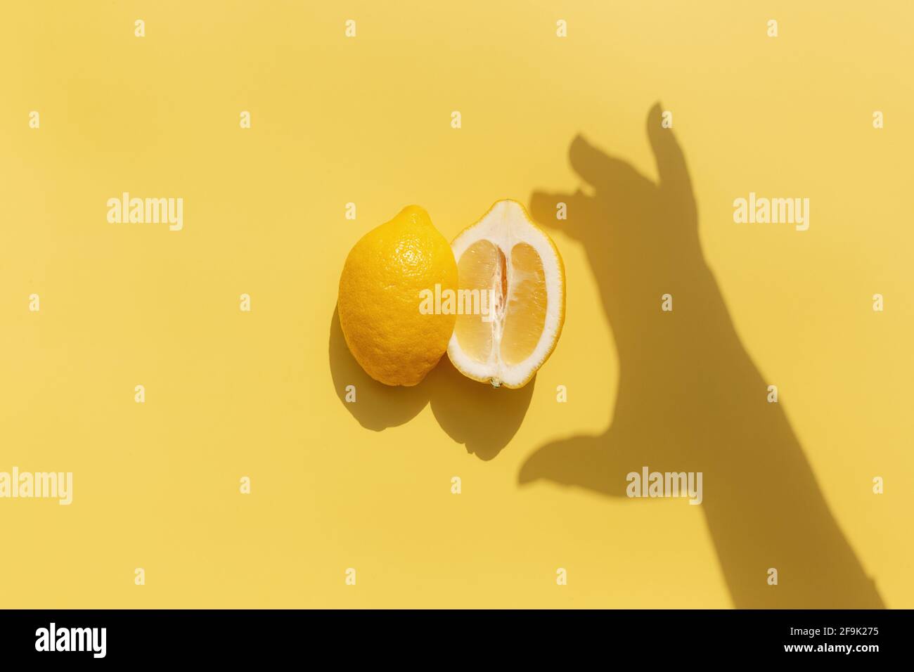 Two halved cuts of lemon with shadow from hand on yellow background ...