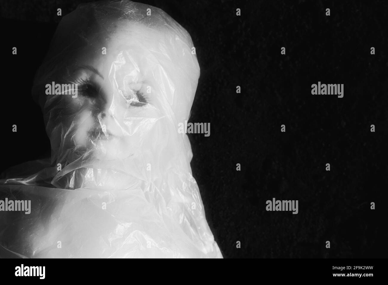Black and white image of female doll trapped wrapped in plastic ...
