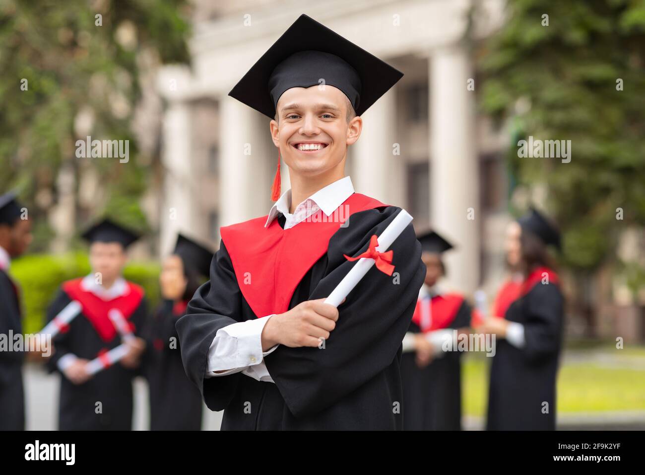 Cheerful guy in graduation costume with diploma posing outdoors Stock ...