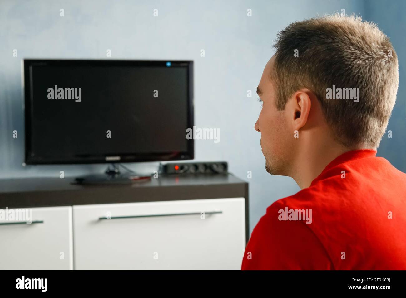 The young guy watches the TV turned off carefully. Single man on the ...