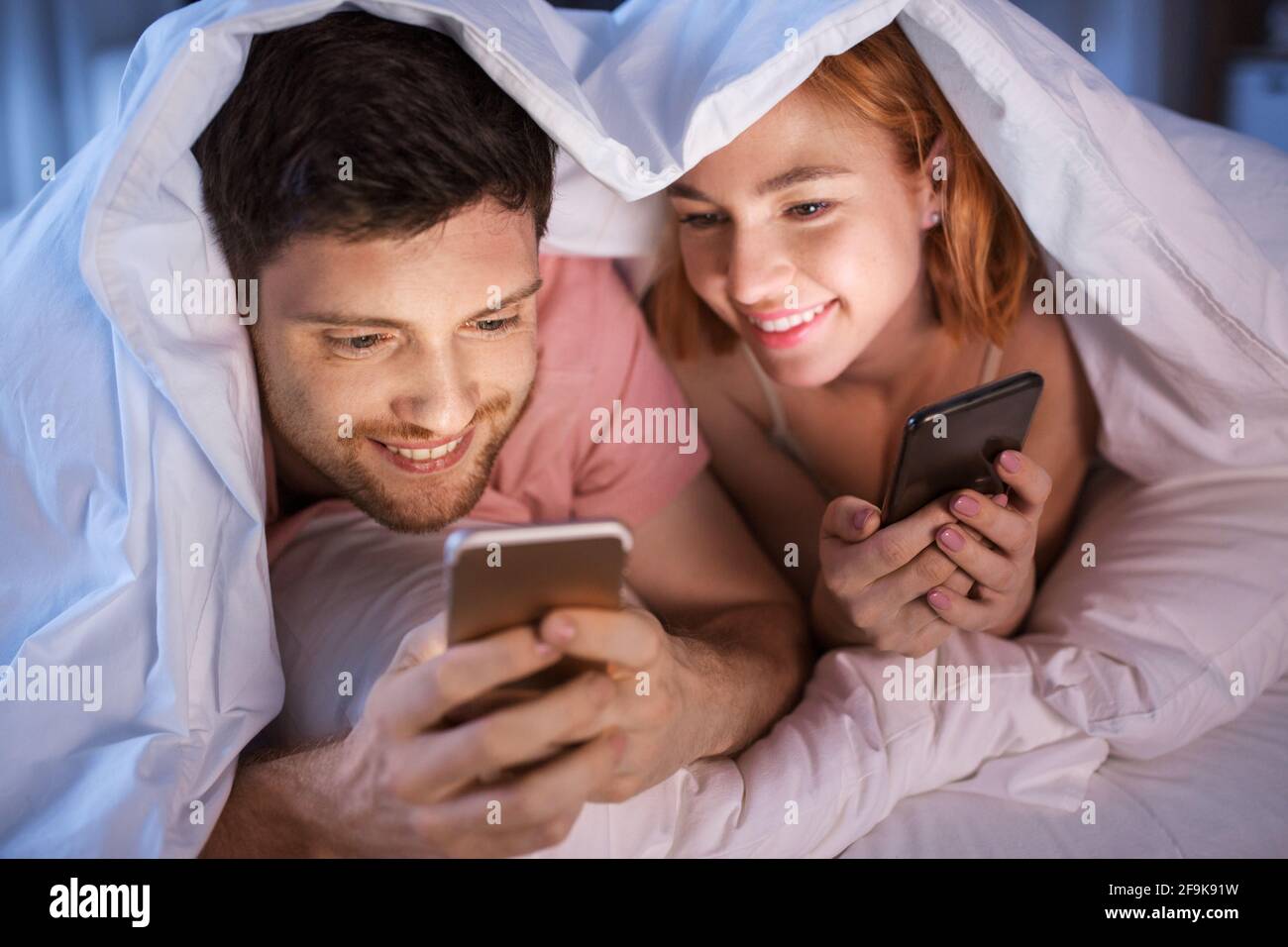 happy couple using smartphones in bed at night Stock Photo - Alamy