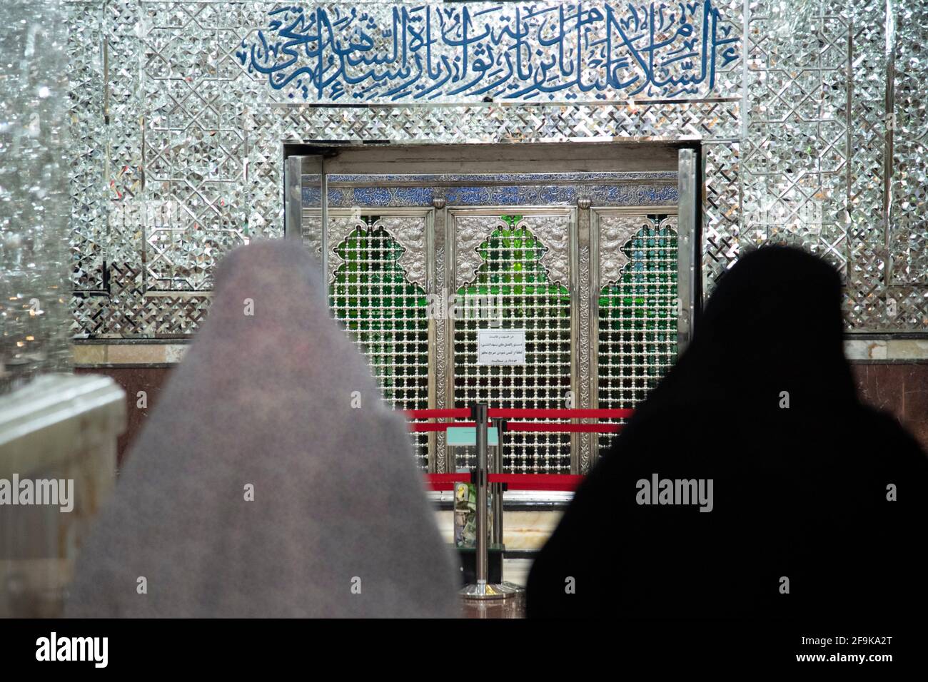 Two woman stand behind the red tape and pray.The shrine of Shah Abdol ...