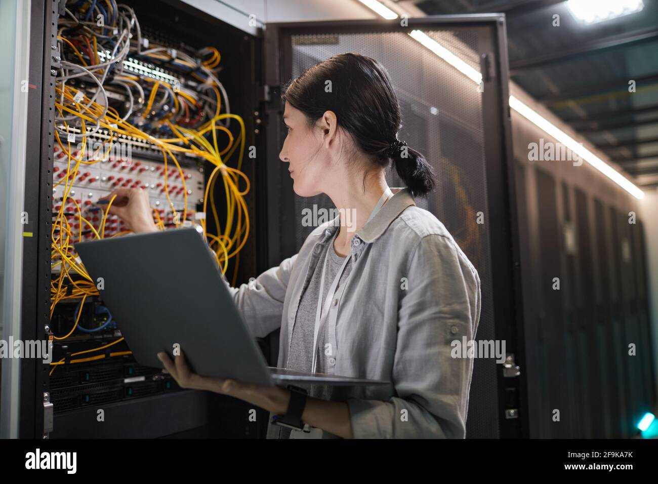 Waist up of female network engineer connecting cables in server cabinet ...