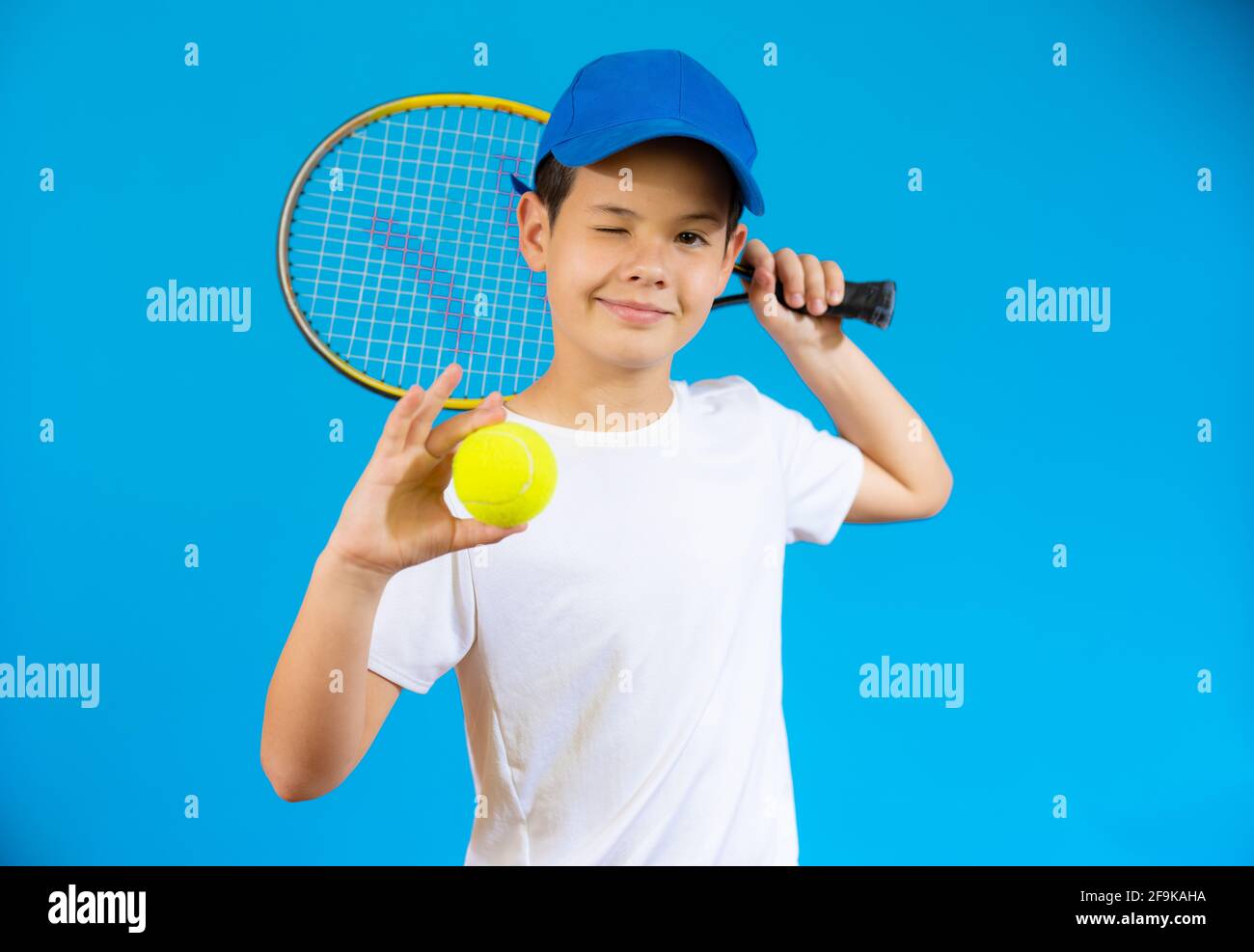 Young boy with tennis racket and ball isolated over blue background ...