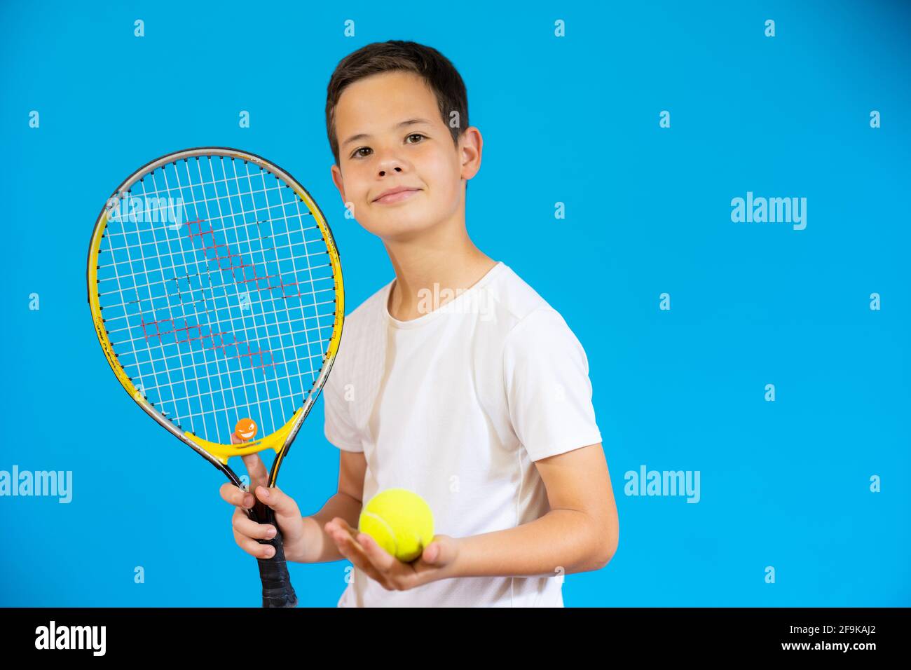 Young boy with tennis racket and ball isolated over blue background ...