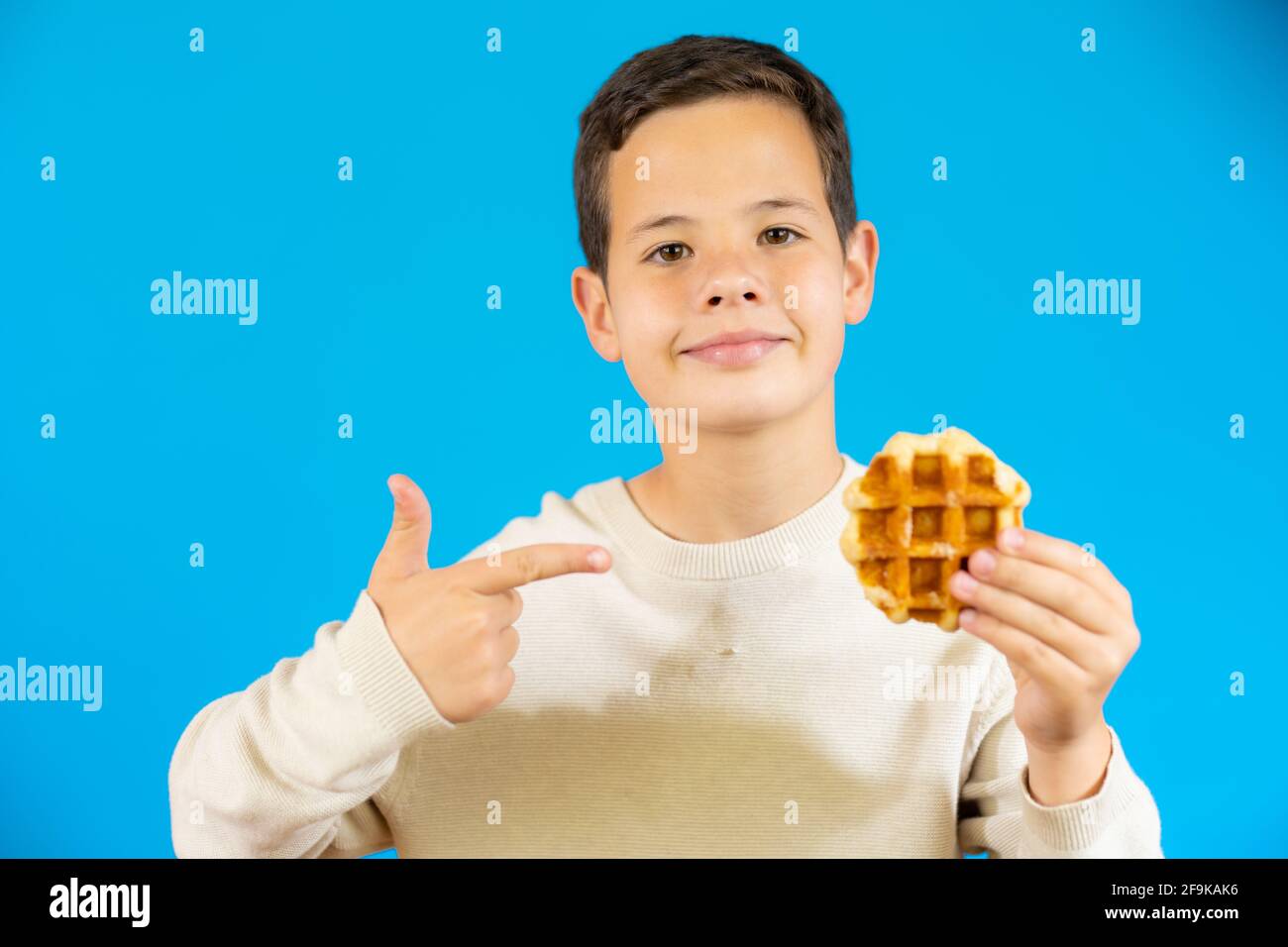 Smiling cute boy eating sweets isolated over blue background Stock ...
