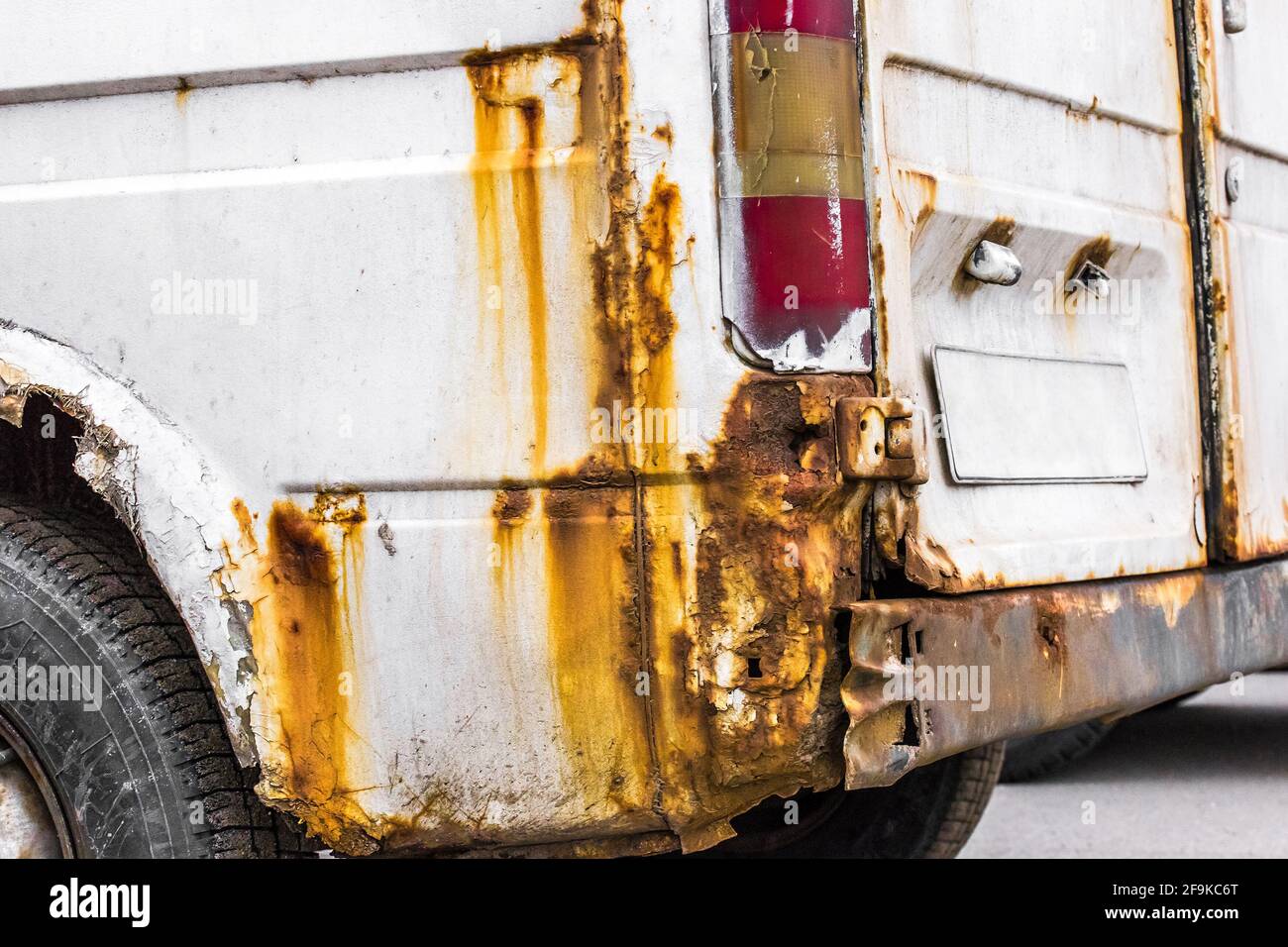 Rust on the rear wing of a white minibus, old rusty car. Depreciation of a automobile or road ...