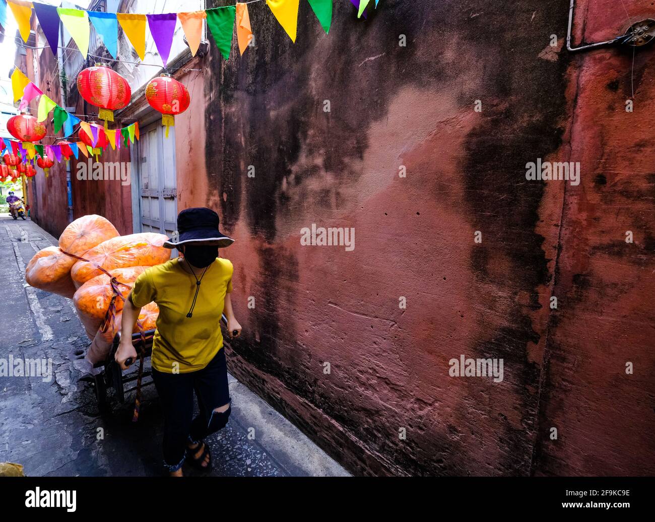 A female porter pulls a trolley laden with goods along a narrow alley ...