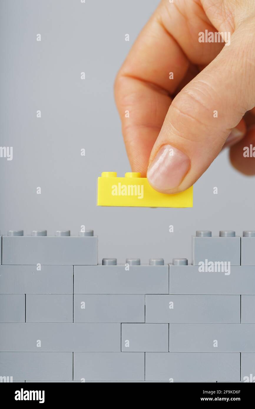 A yellow brick puts a hand on a toy gray wall. The concept of building ...