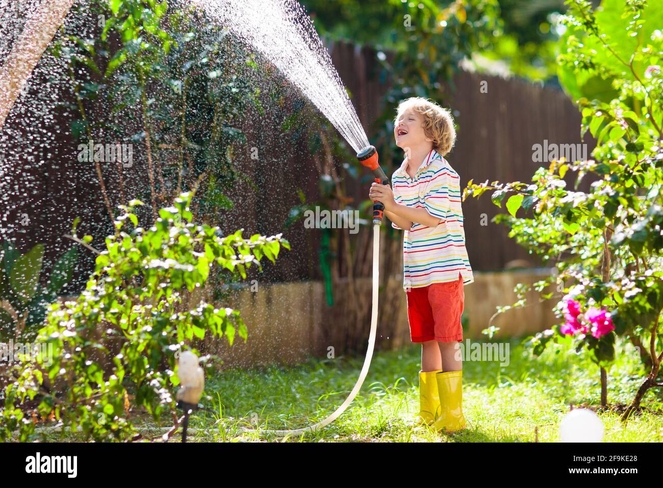 Child watering flowers and plants in garden. Kid with water hose in ...