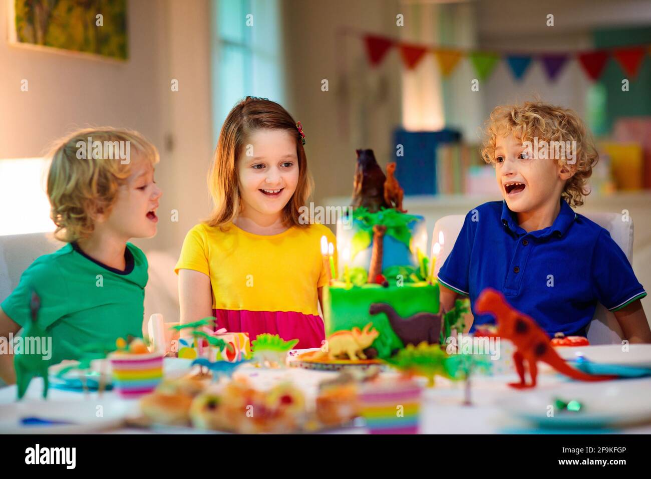 Kids birthday party. Dinosaur theme cake. Little girl blowing candles ...