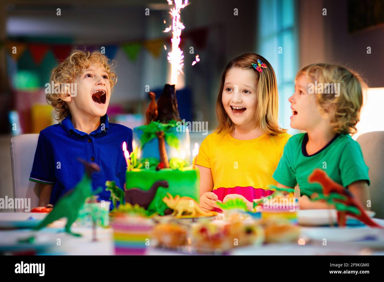 Kids birthday party. Dinosaur theme cake. Little girl blowing candles ...