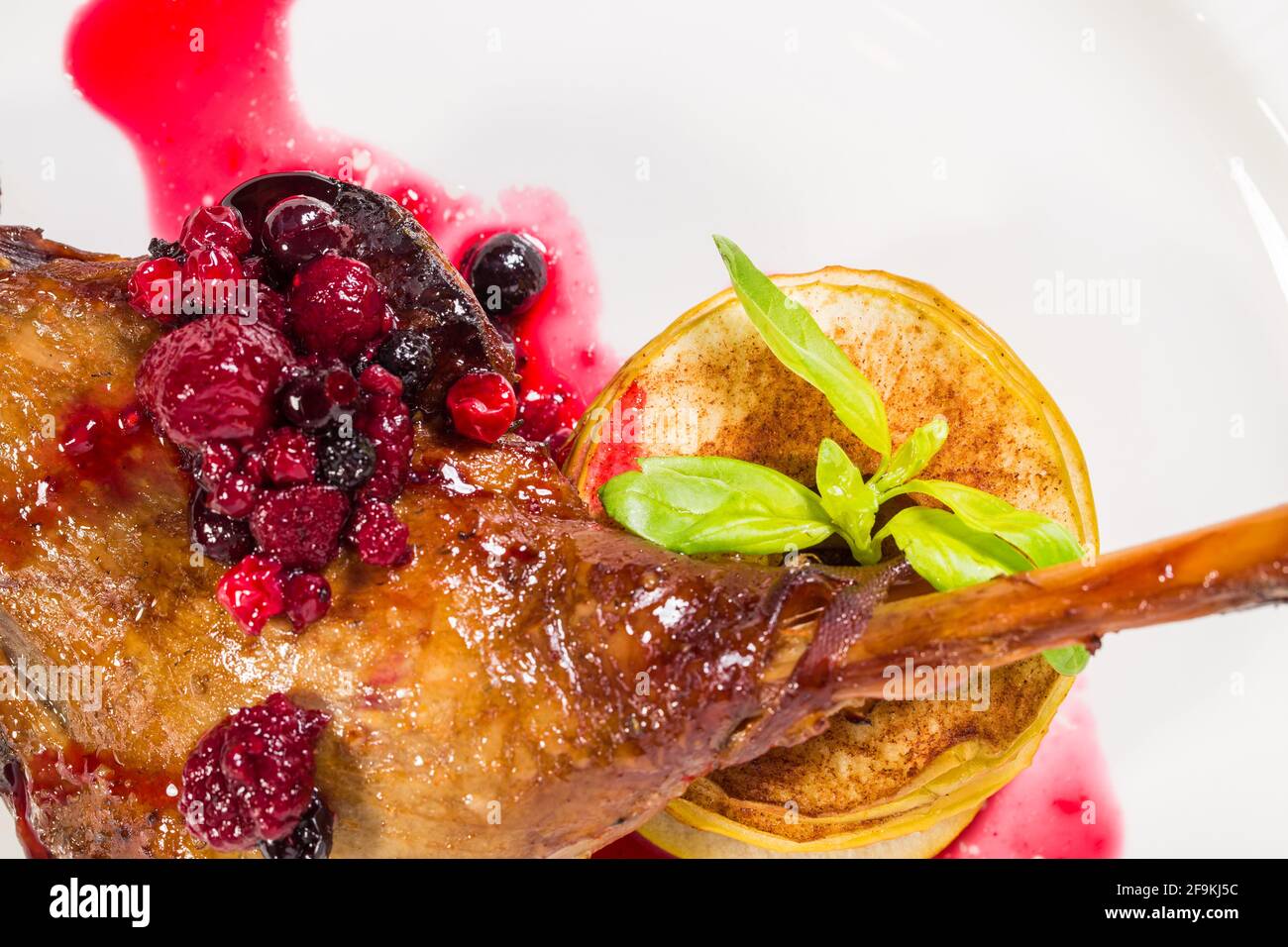 Delicious duck leg confit with red berry sauce and baked sliced apple ...