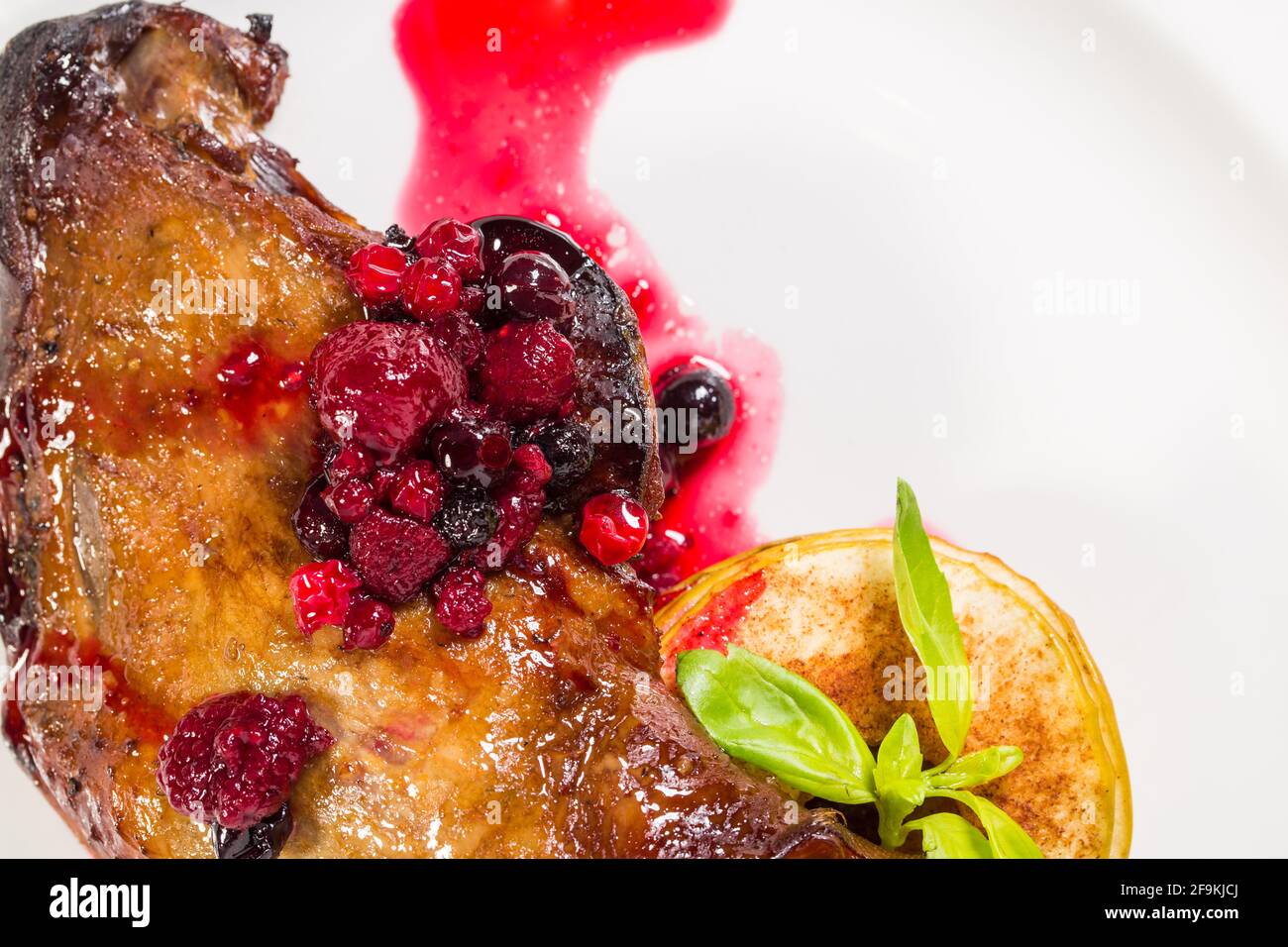 Delicious duck leg confit with red berry sauce and baked sliced apple ...