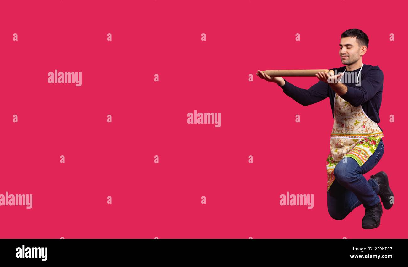 Brunette man, caucasian wearing chef apron kneeling holding rolling pin ...