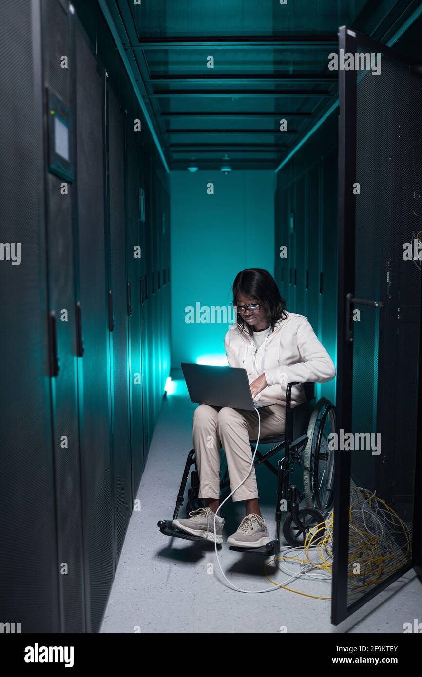 Vertical full length portrait of disabled African-American woman using laptop while working in ...