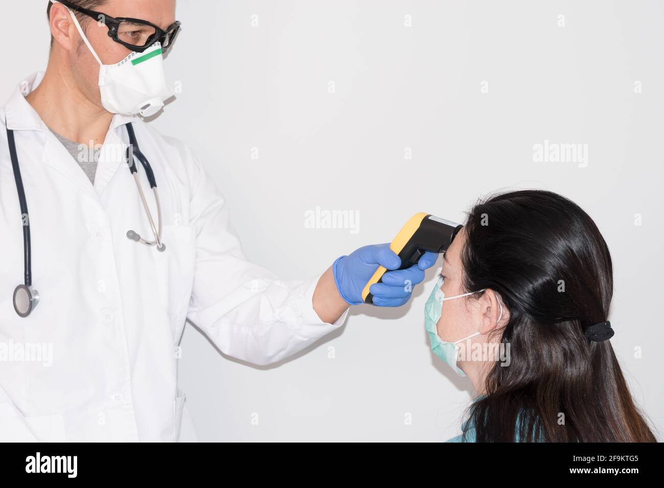 Doctor measuring a young patient's forehead temperature with a laser ...