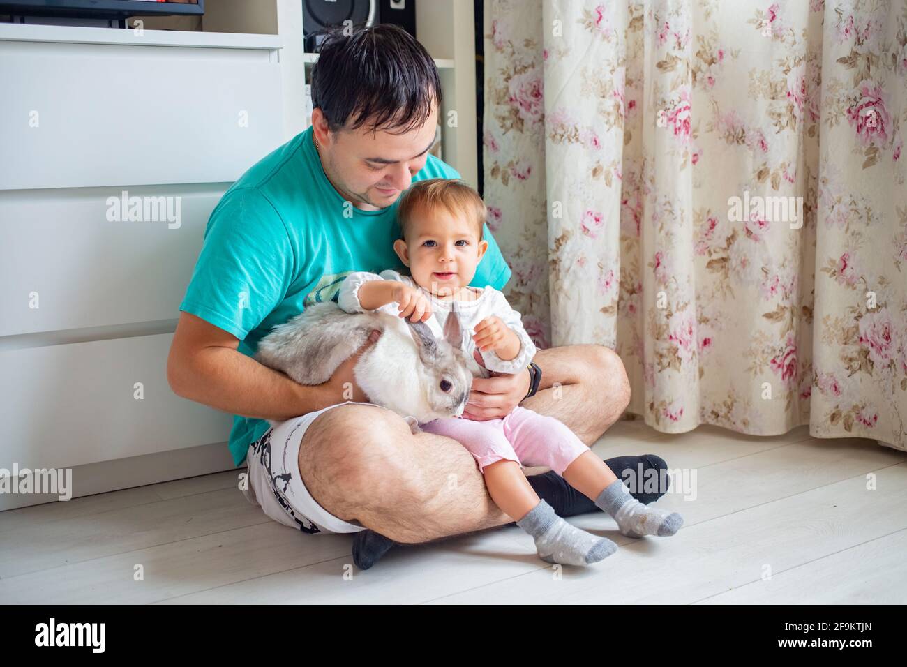 adorable baby sits in dad's arms and strokes a decorative rabbit ...
