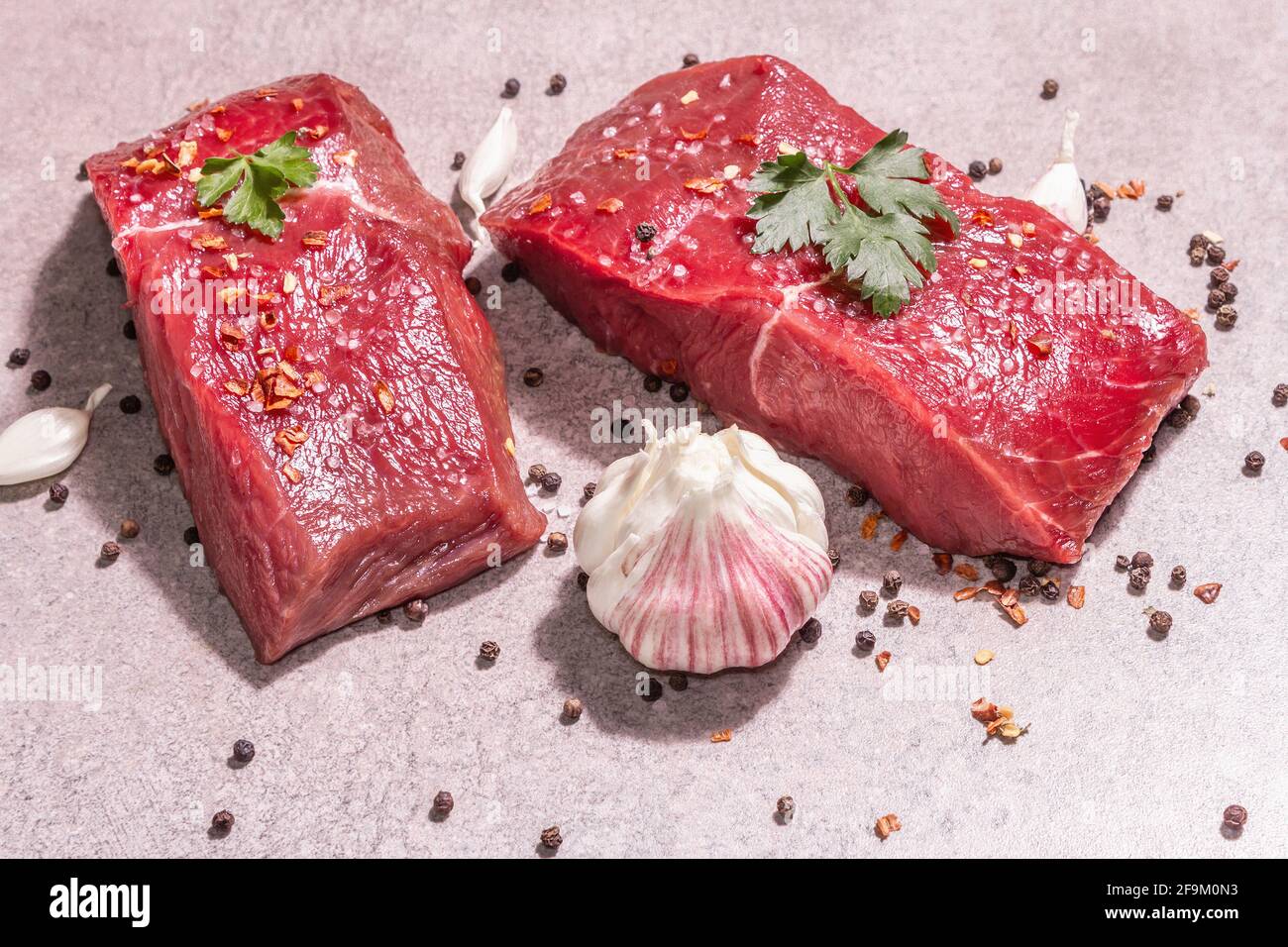Raw beef steaks on a grey stone background. Trendy hard light, dark ...