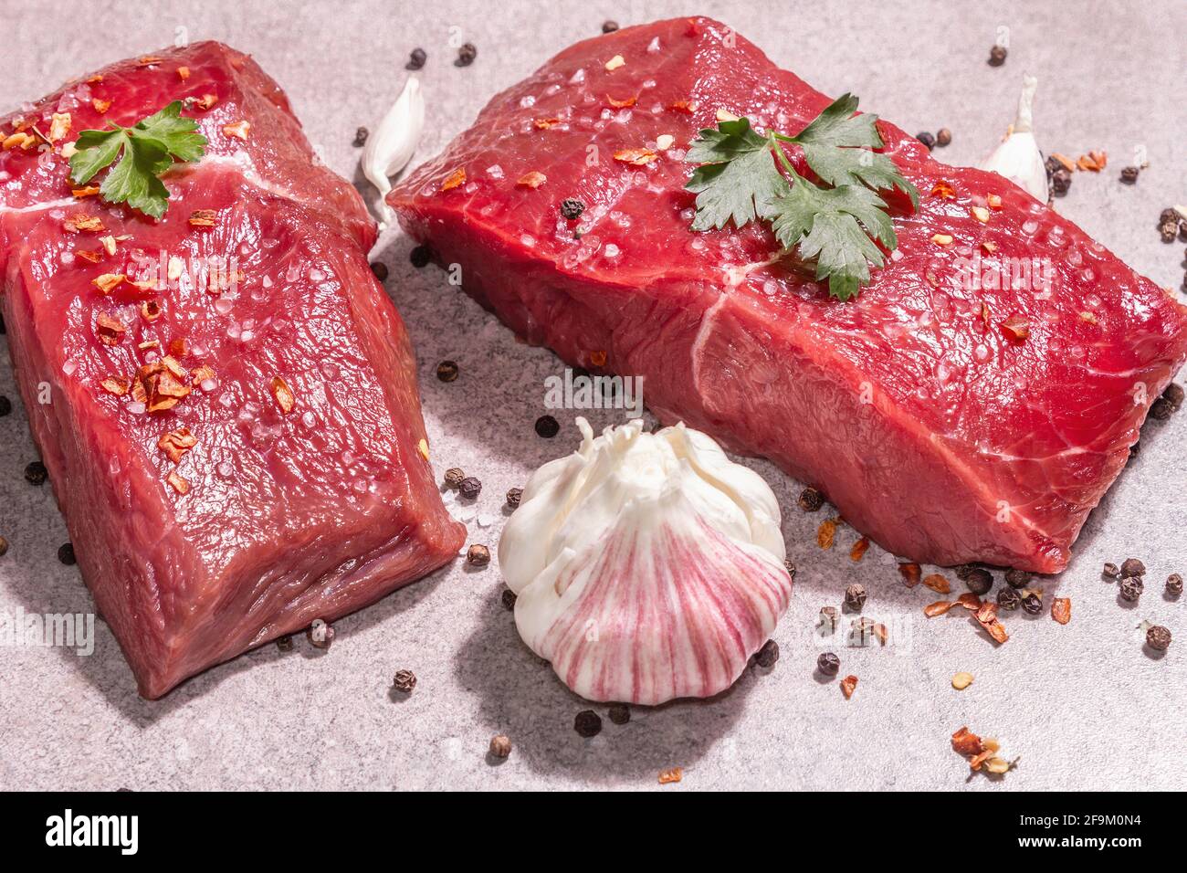 Raw beef steaks on a grey stone background. Trendy hard light, dark ...