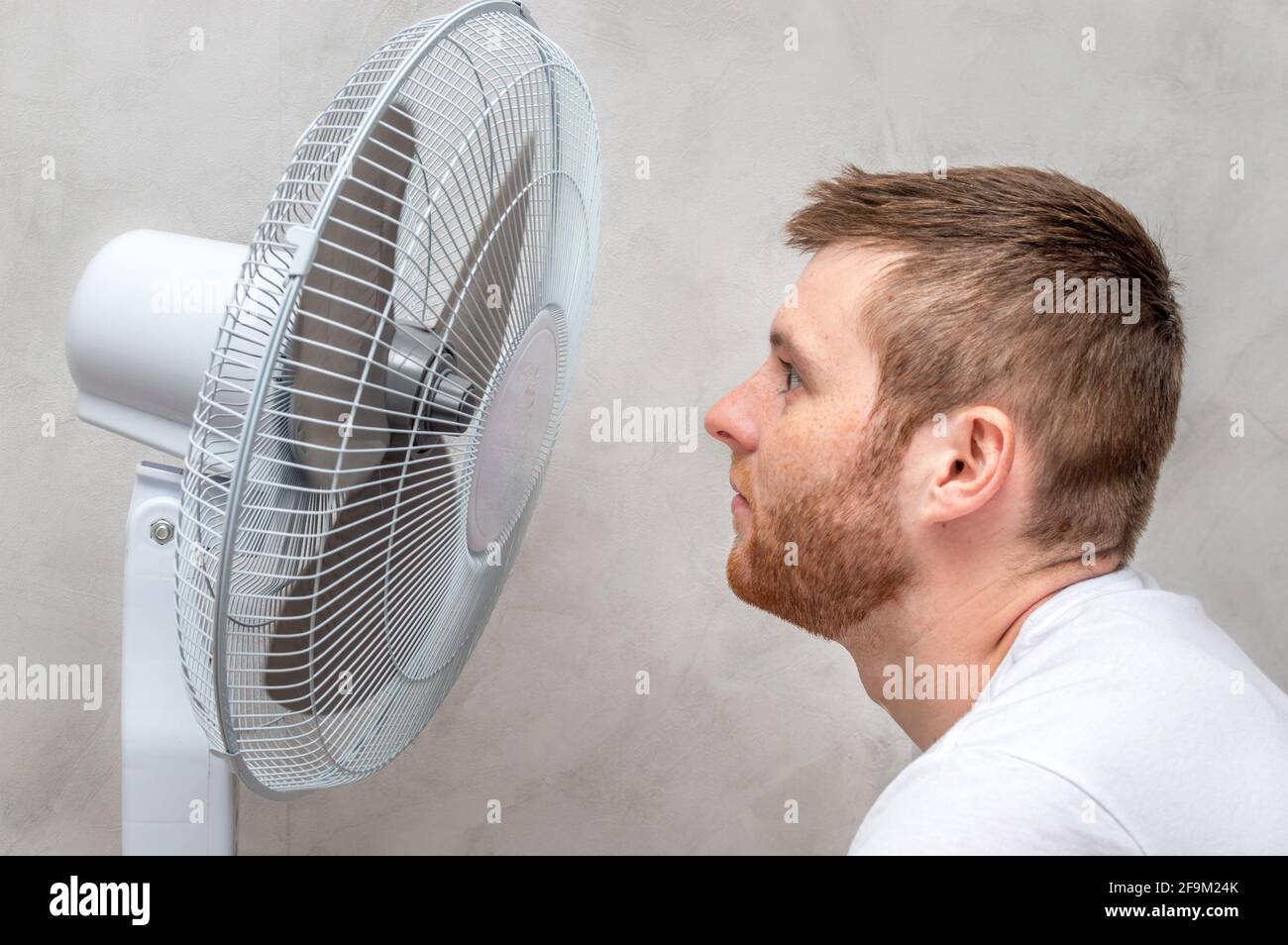 young man stands by the fan. Close-up portrait. The man is hot in the ...