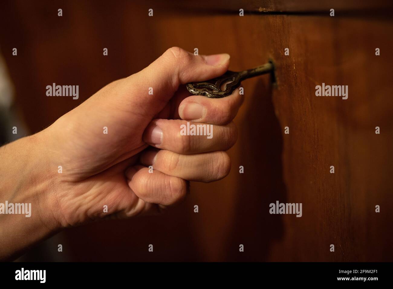 Hand holding a rusty old key to put it in the lock of a wooden door ...