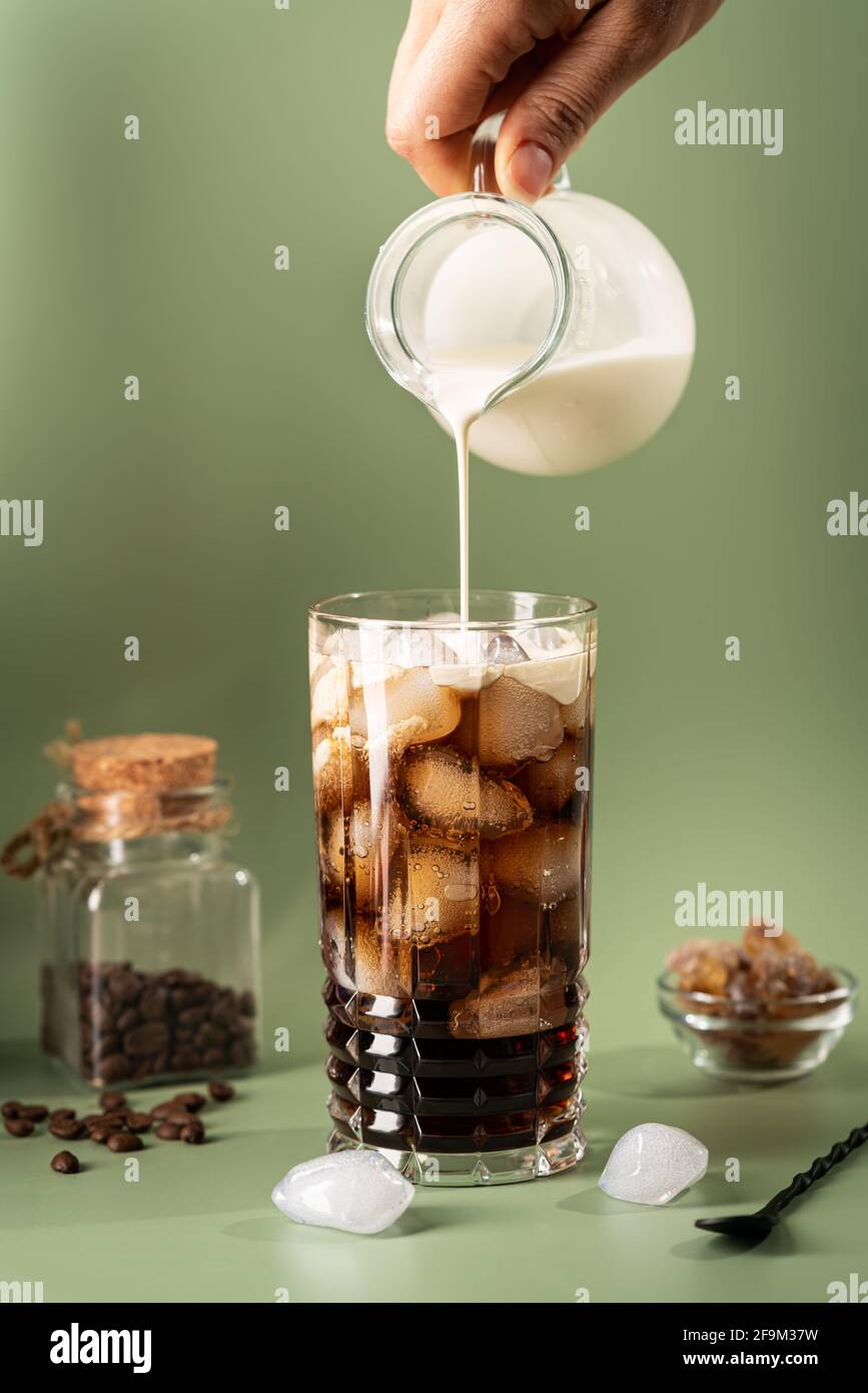 Pouring cream into a glass with iced coffee on green background Stock ...